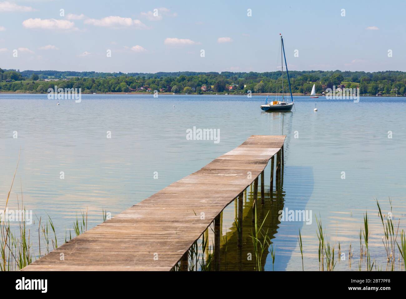 Wooden pier and sailboat at Ammersee (Lake Ammer). Clear sky with a few ...
