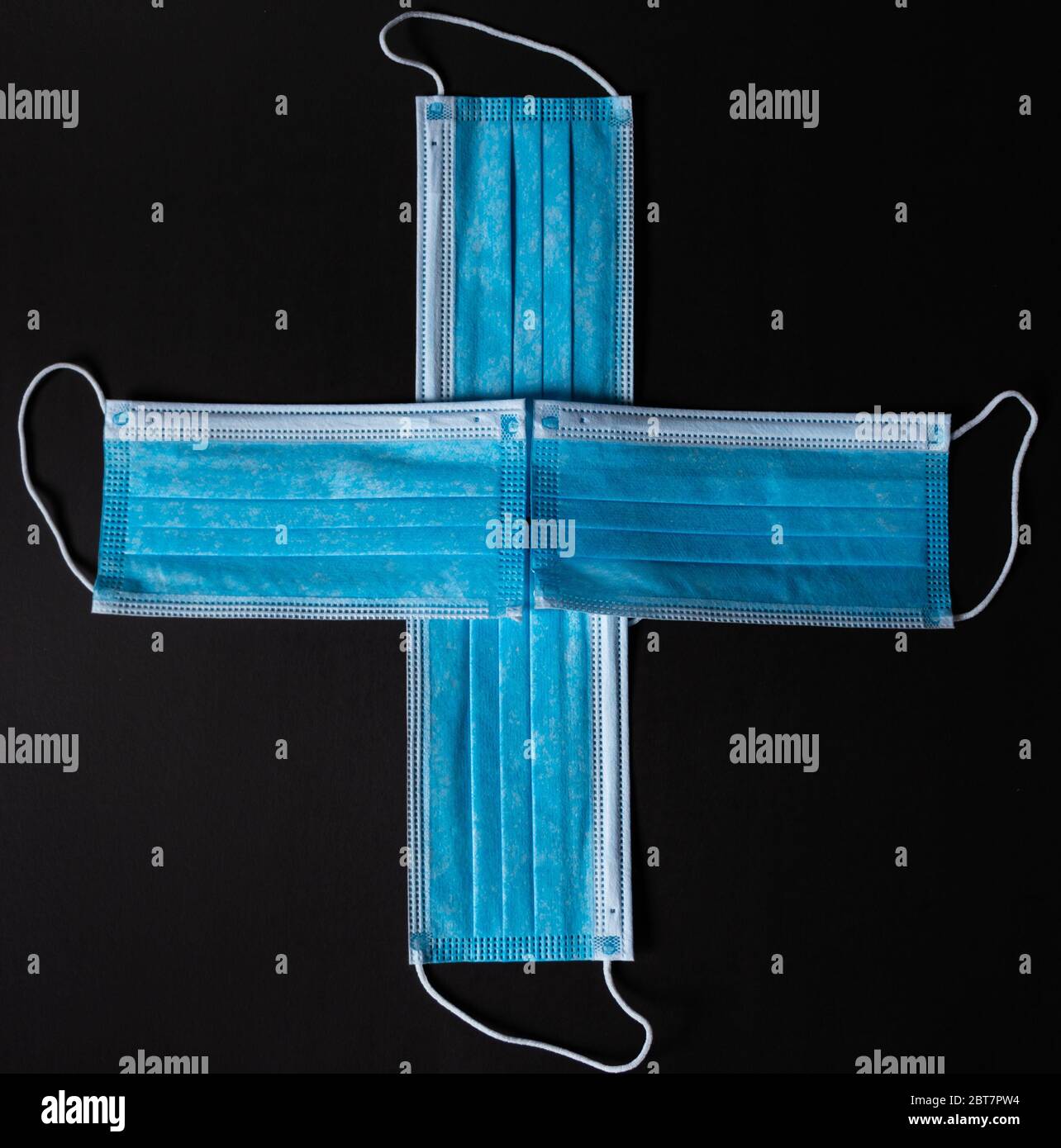 Four surgical face masks put together as a cross in black background ...