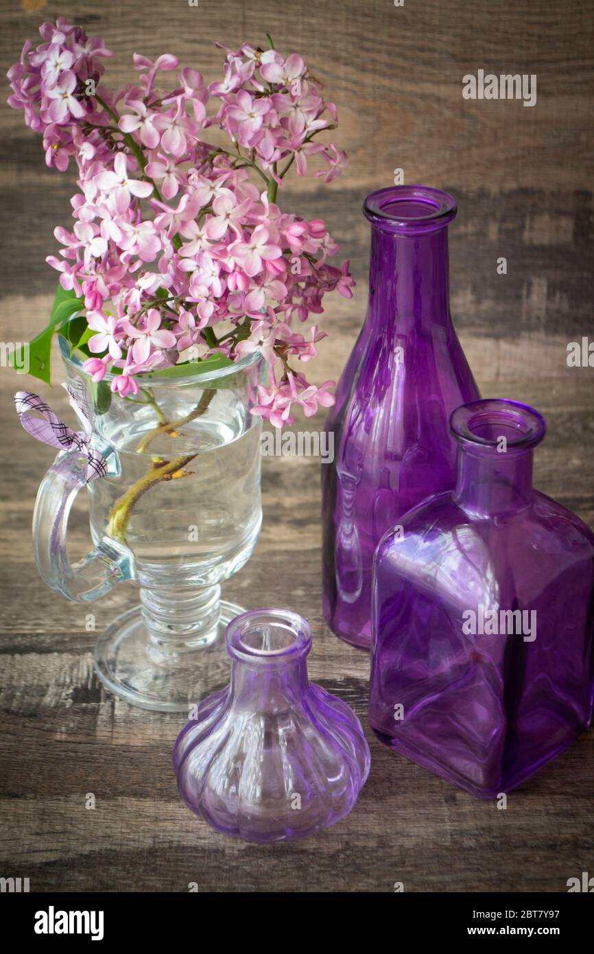 branch of blooming lilac in a glass bottle with violet bottles ...