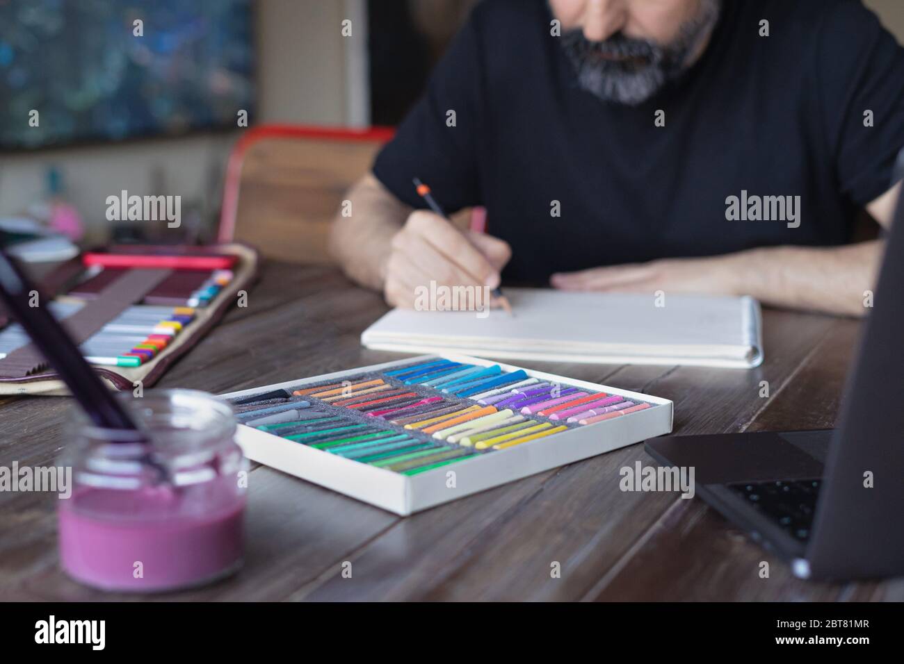 man artist painting with pencil and pastel crayon on paper in front of ...