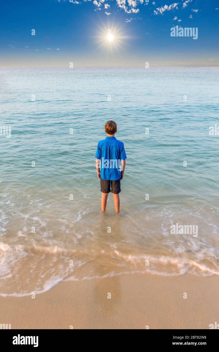 Young boy staring our towards to the horizon with his feet in the surf ...