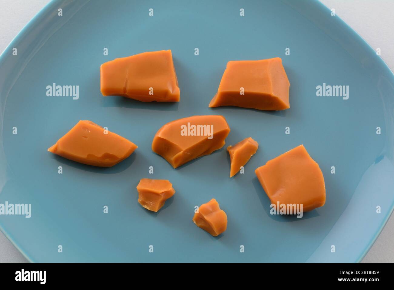 Banana toffee candy shard pieces on blue plate on white background ...