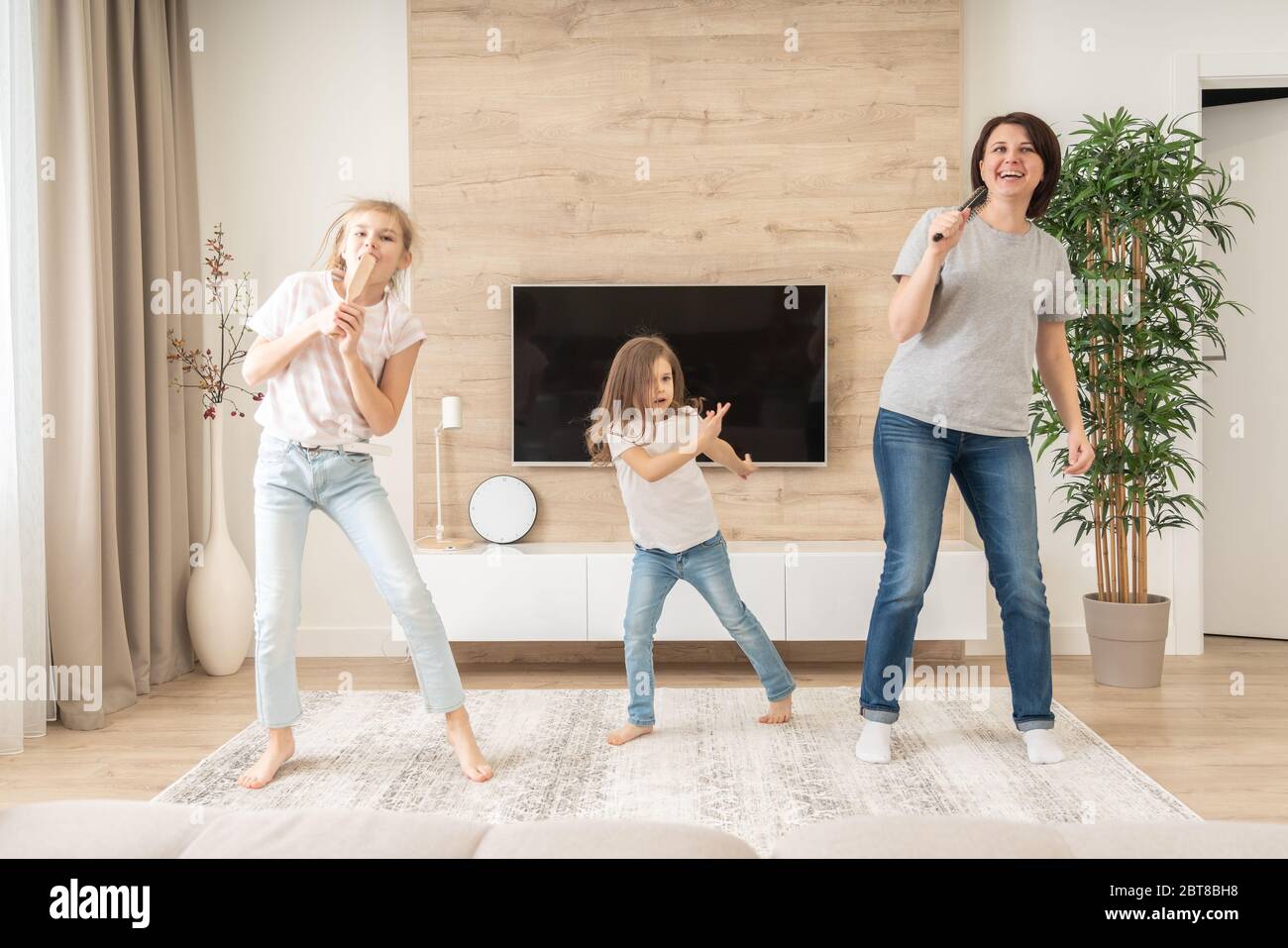 Happy mother and two daughters having fun singing karaoke song in hairbrushes. mother laughing ...