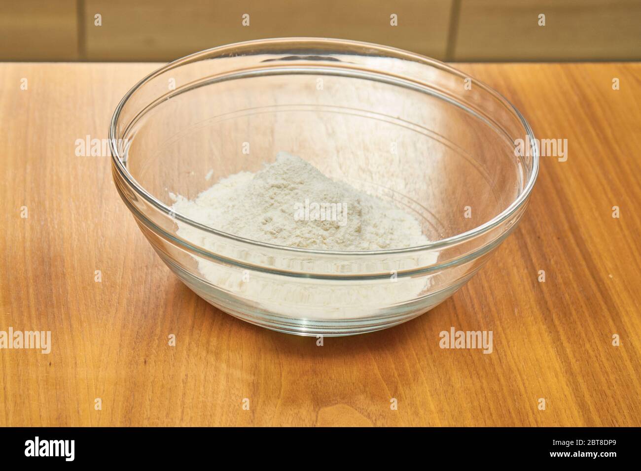 Pile of flour in a transparent glass salad bowl on wooden table front ...