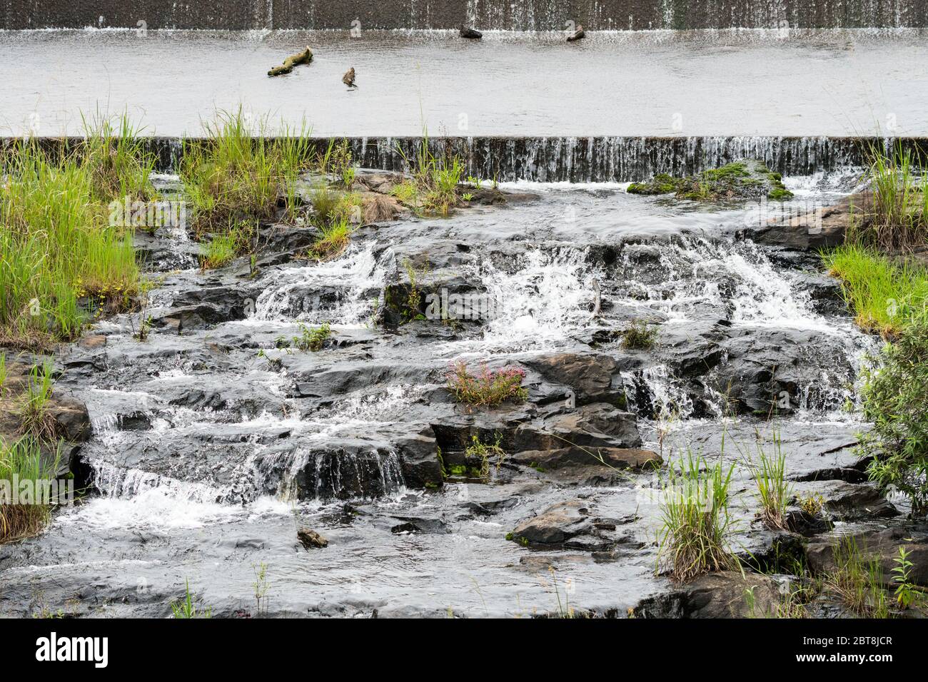 weir with water cascading over rocks and narrowing into a small stream ...