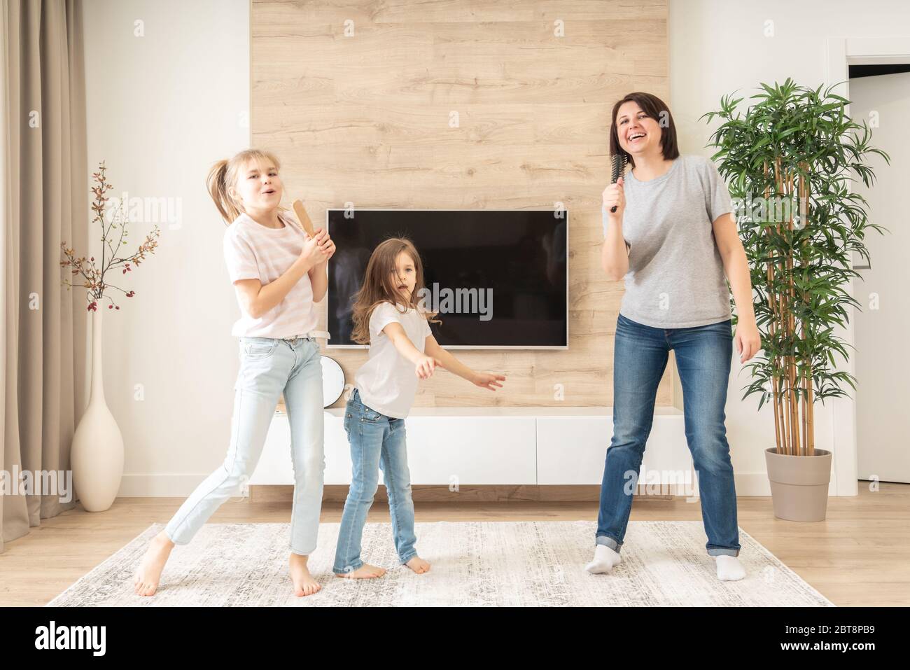 Happy mother and two daughters having fun singing karaoke song in hairbrushes. mother laughing ...