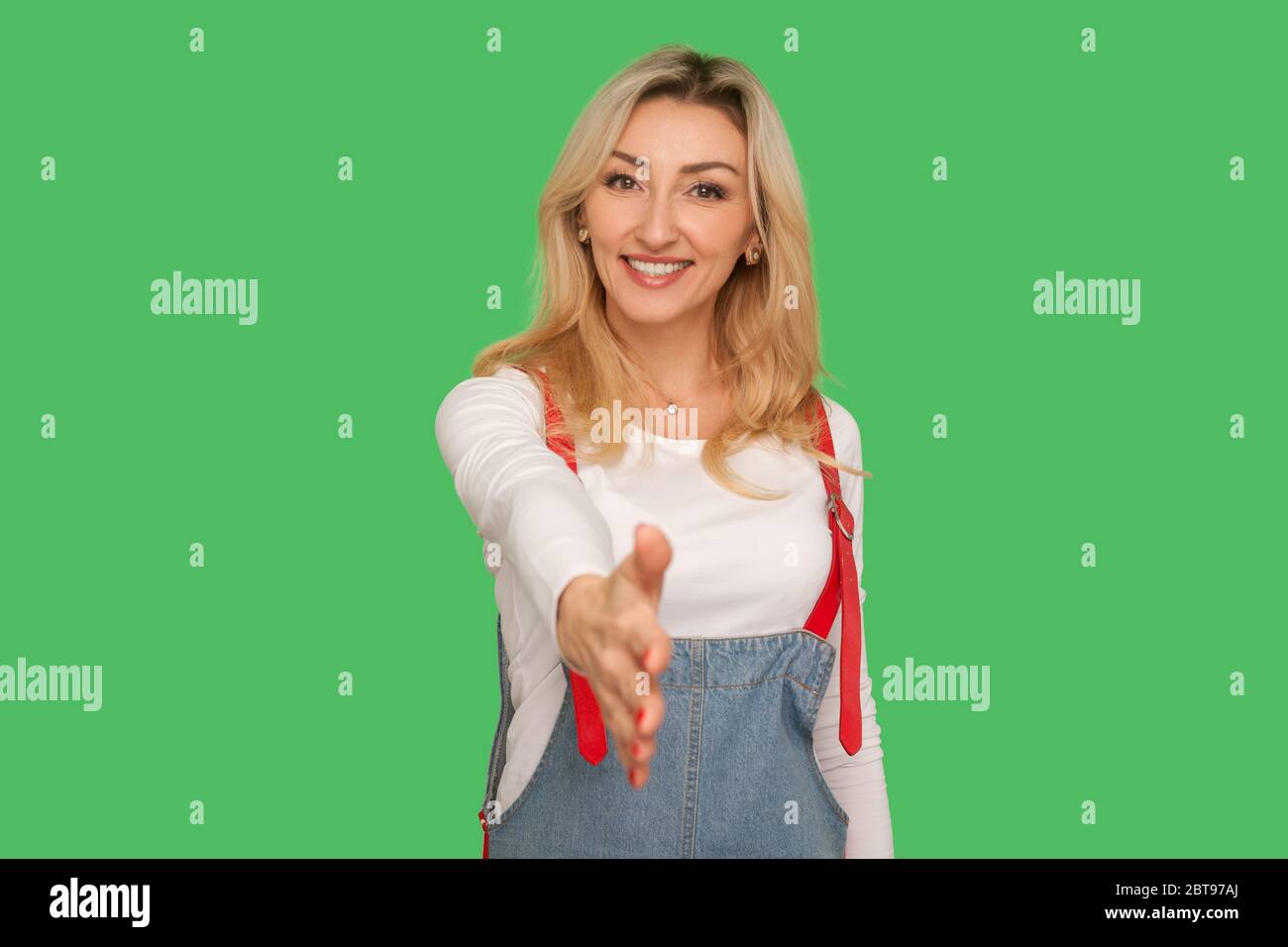 Portrait of amiable adult blond woman in stylish denim overalls ...