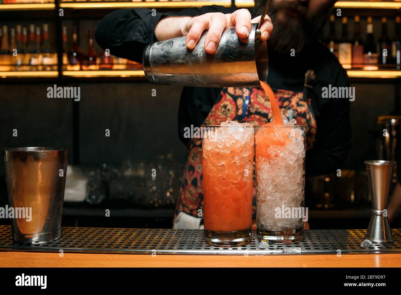 A professional bartender makes two red cocktails, pouring a cocktail ...