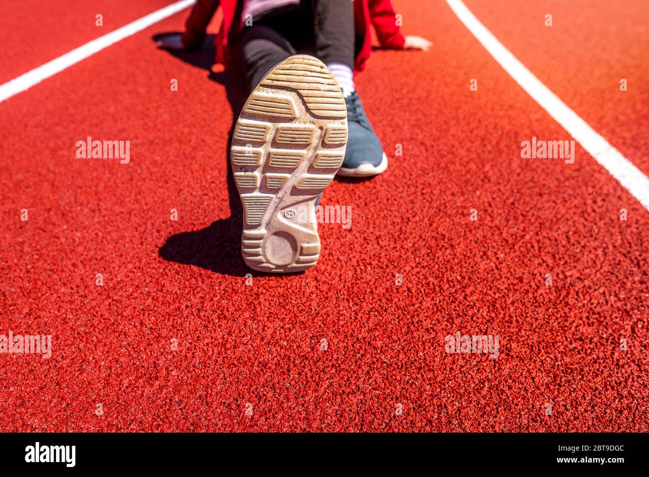 Girl sit on the running track in stadium, rest and relax after exercise ...