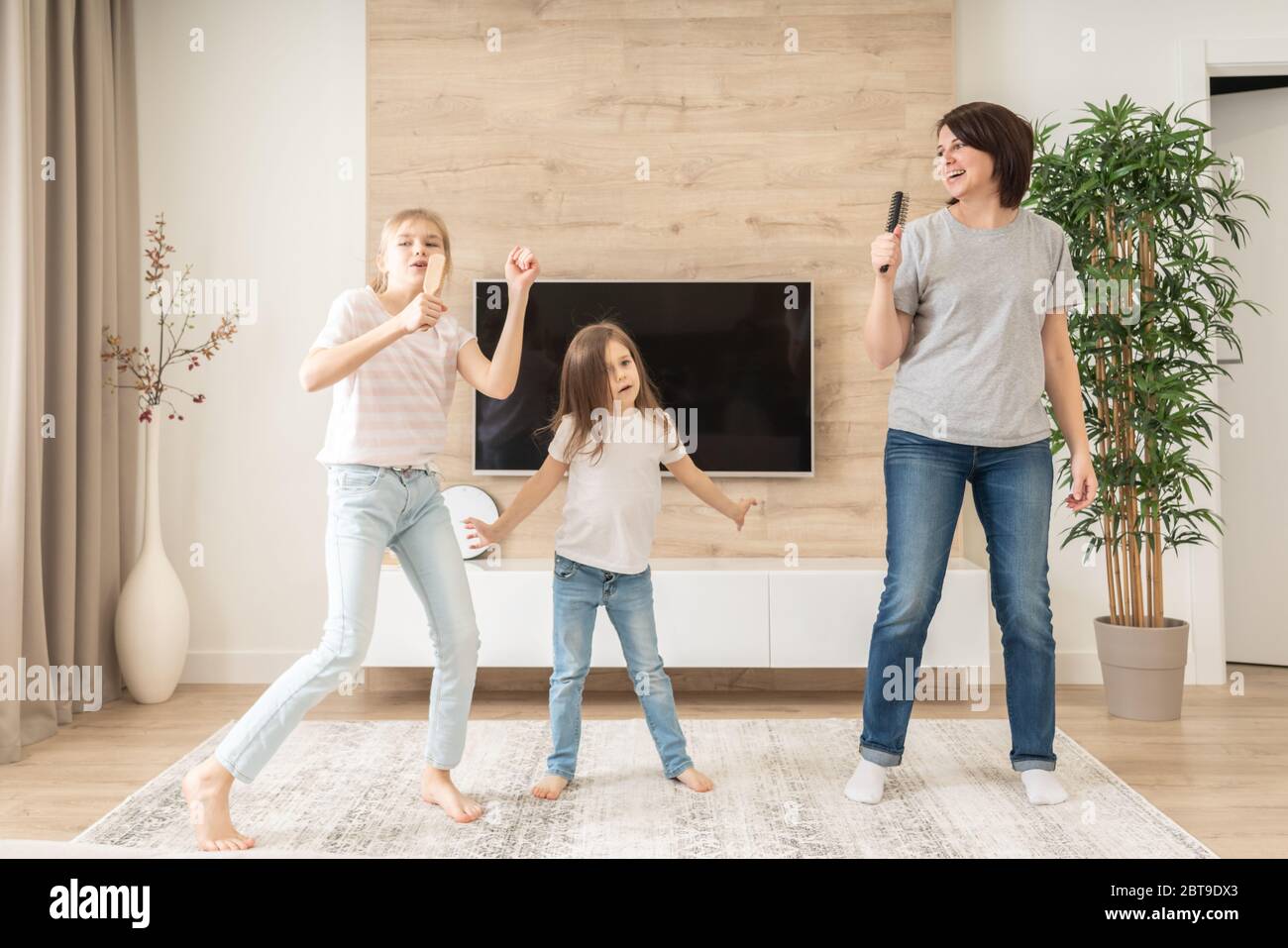 Happy mother and two daughters having fun singing karaoke song in hairbrushes. mother laughing ...