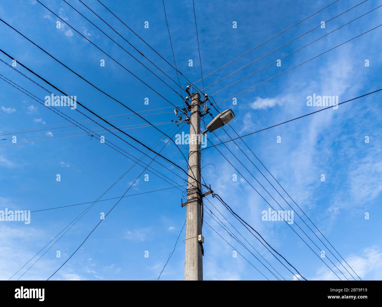 Concrete lamp post with many cables connected radially on blue sky with ...
