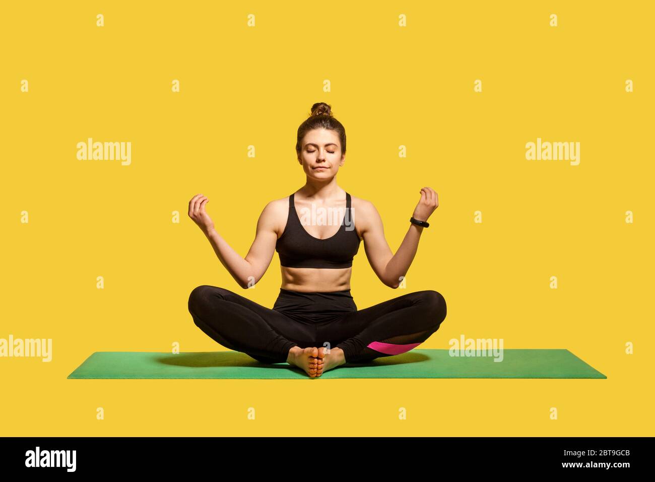 Concentrated Calm Woman With Hair Bun In Tight Sportswear Sitting In