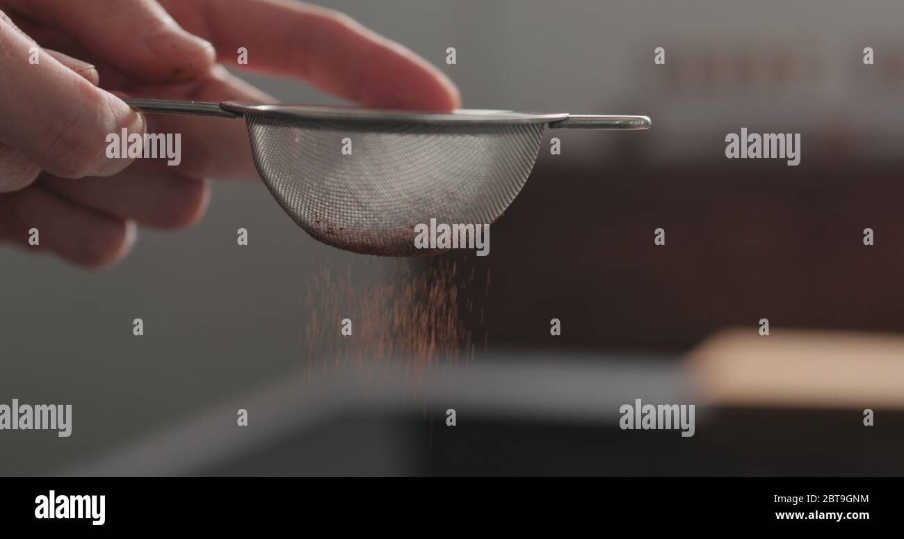 man hand sprinkle cocoa powder from sieve Stock Photo - Alamy