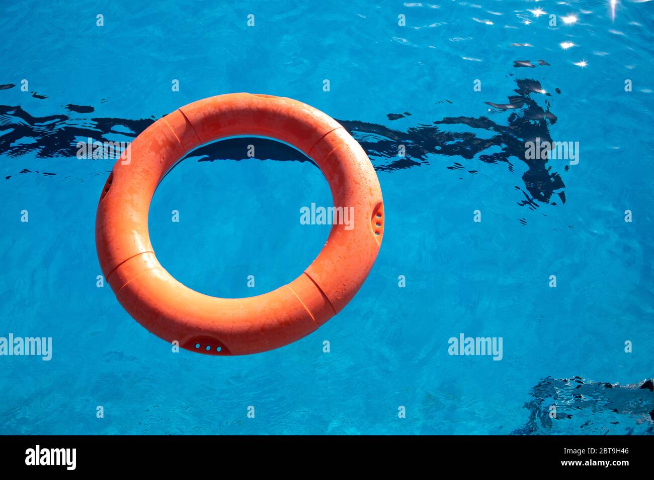 Orange lifebuoy floating on the surface of blue water in a pool Stock ...