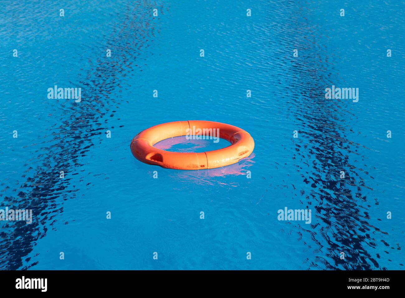 Orange lifebuoy floating on the surface of blue water in a pool Stock ...