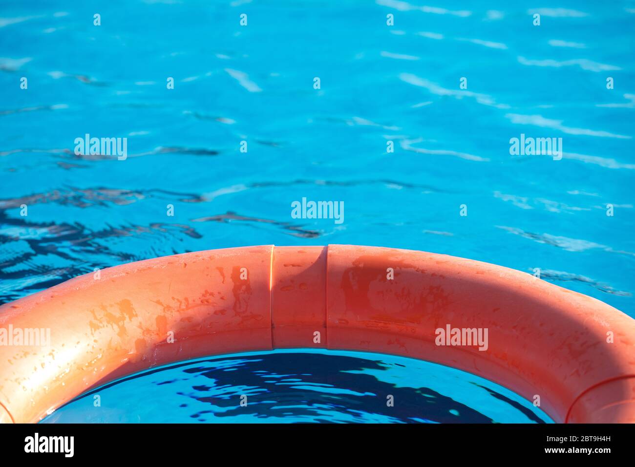 Orange lifebuoy floating on the surface of blue water in a pool Stock ...