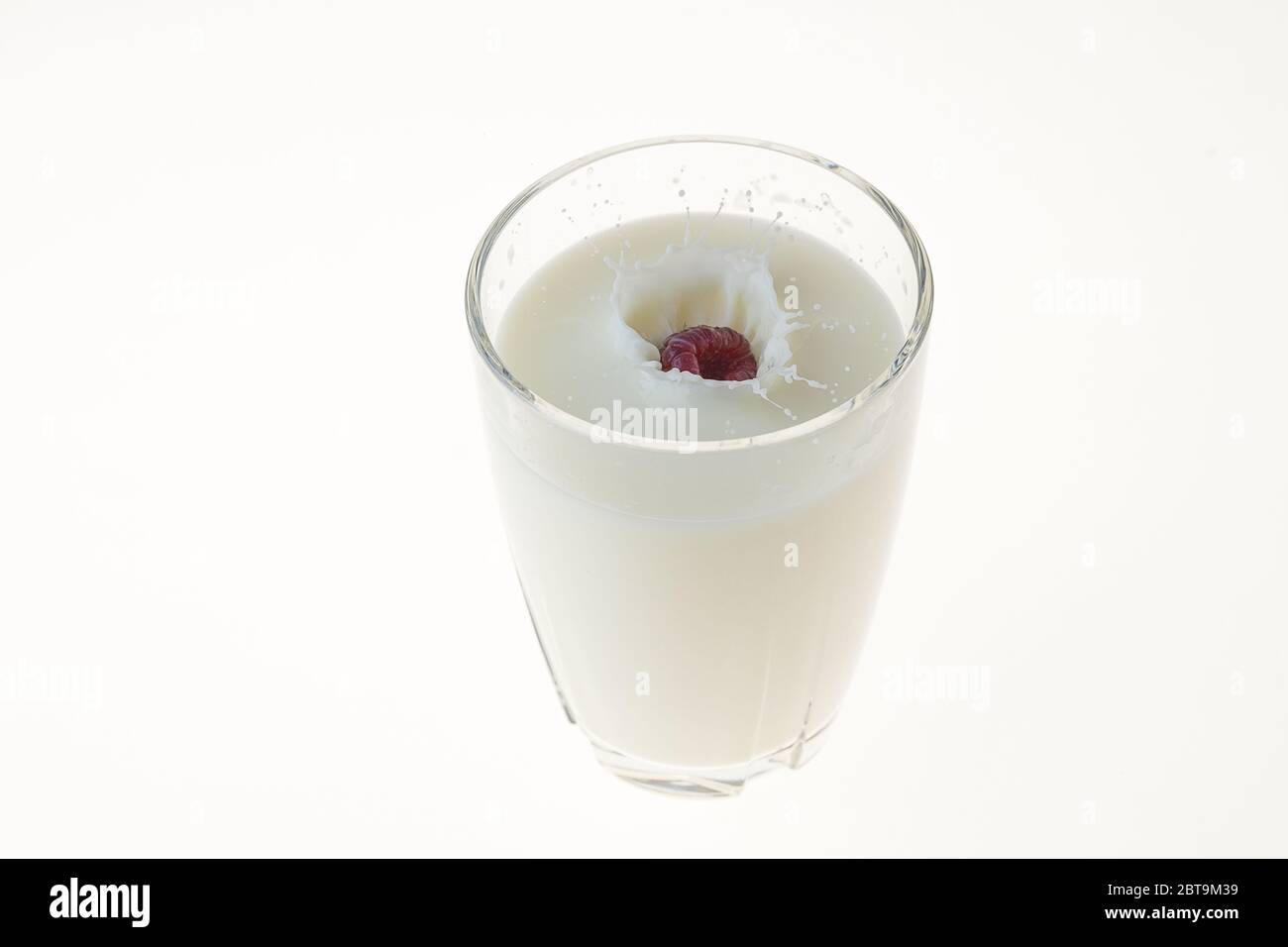 Close up view of red raspberry falling into milk on a white background ...