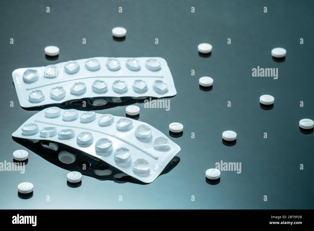 Empty blister packs, white disk-shaped tablets on black mirror ...