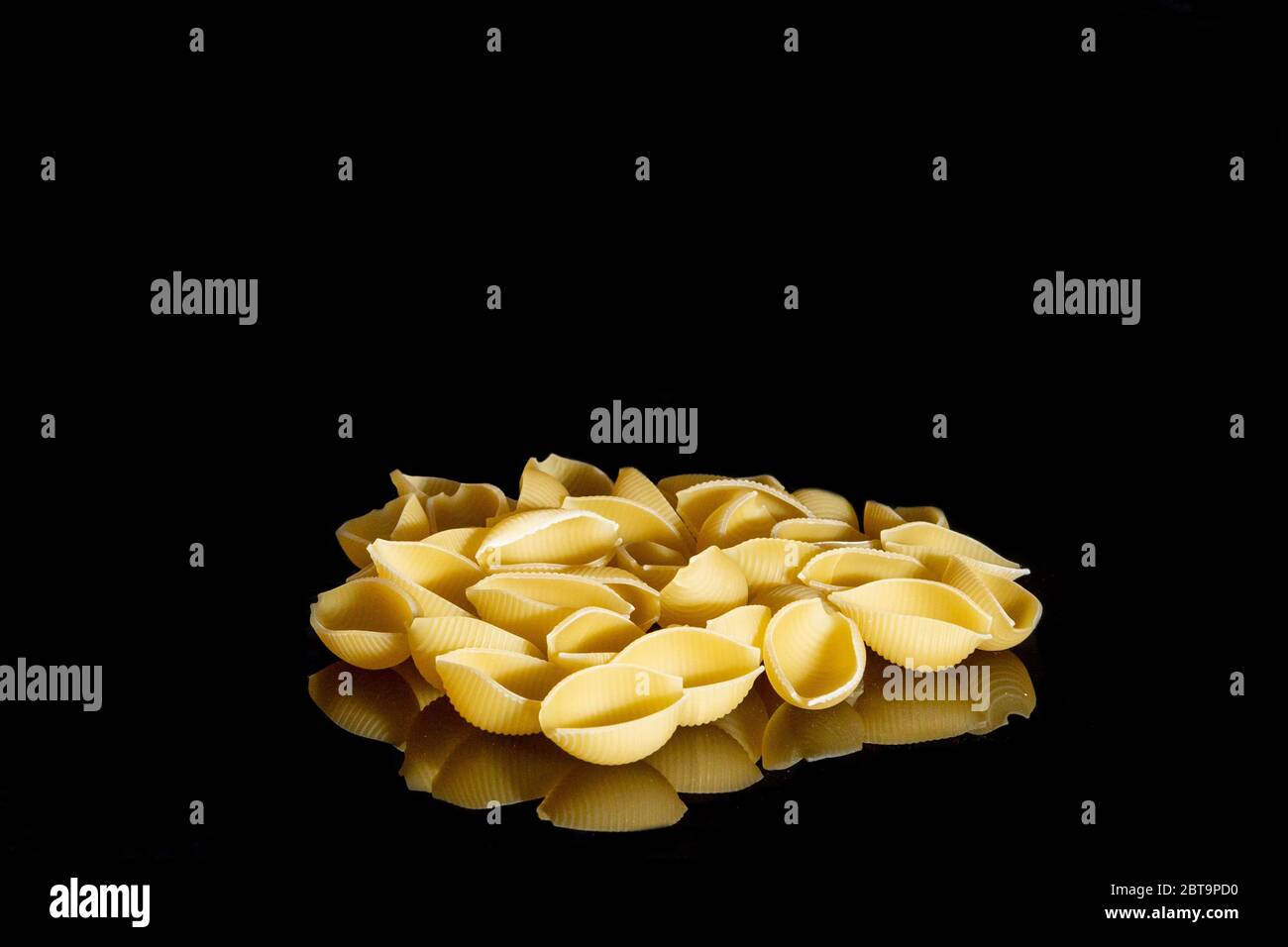 Conchiglie rigate. Pile of raw striped shell pasta isolated on black ...