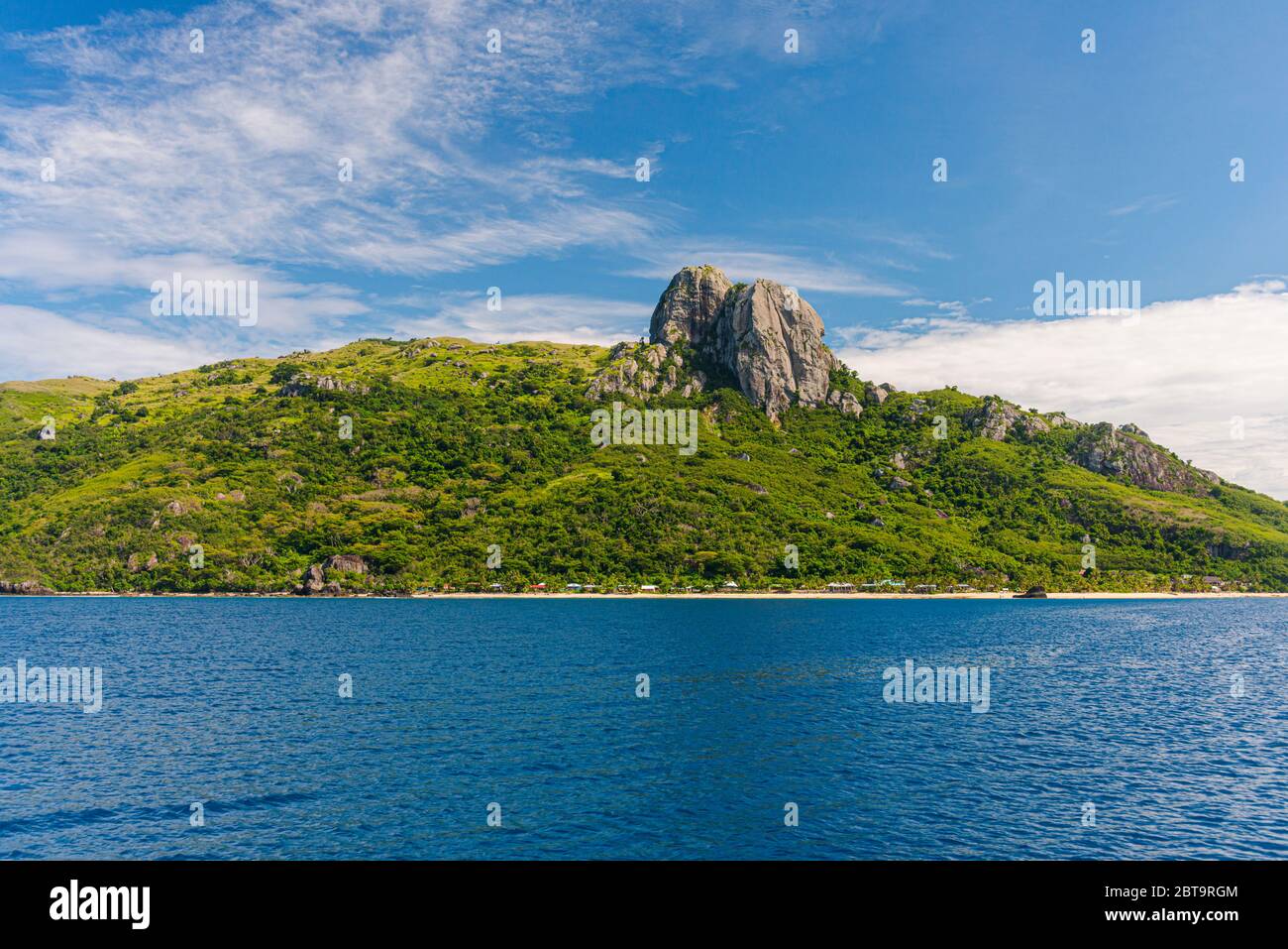 Tropical island with a rocky mountain in a forest. Deep blue water in ...
