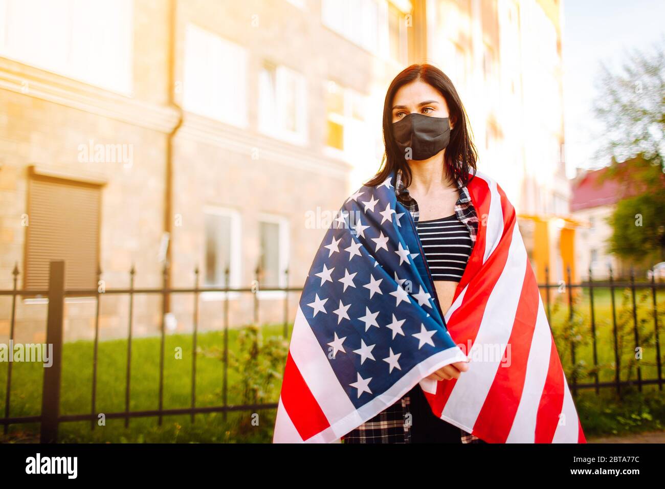 Girl in protective black medical mask wrapped in american flag ...