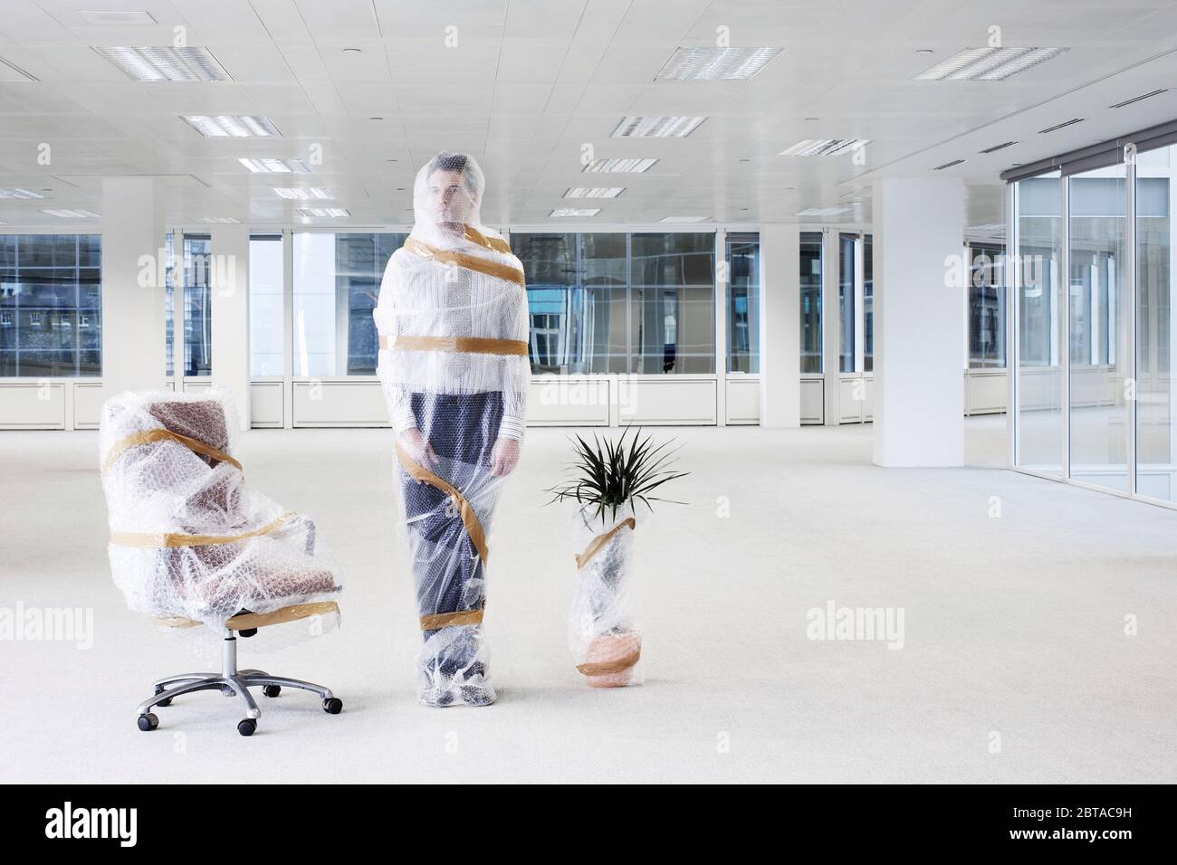 Businessman wrapped in bubble wrap in new office Stock Photo - Alamy