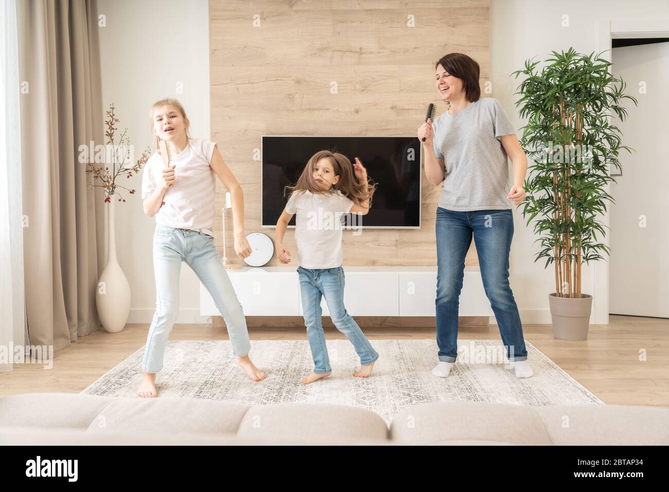 Happy mother and two daughters having fun singing karaoke song in hairbrushes. mother laughing ...