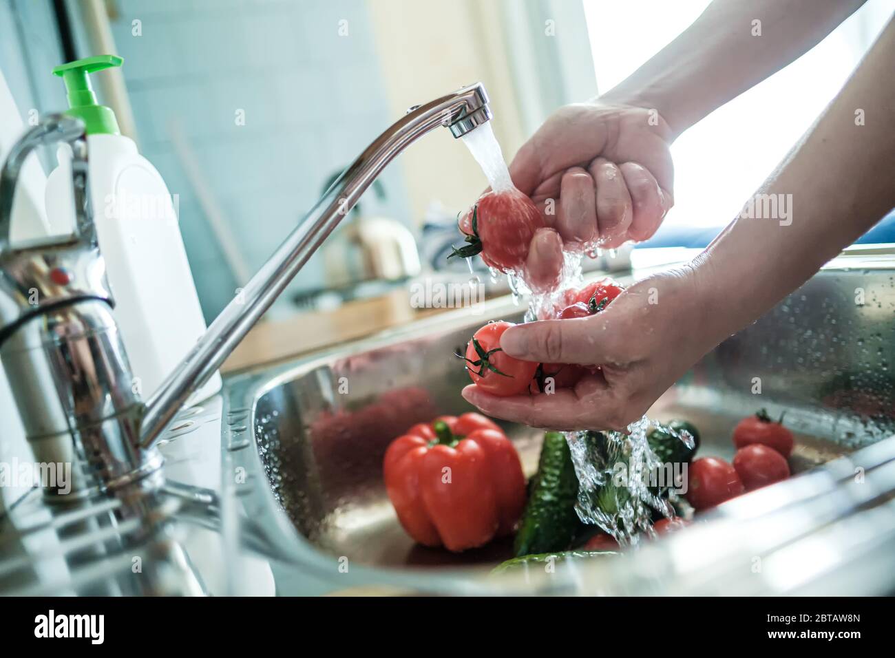 Female hands wash red tomatoes under a stream of water, against the ...