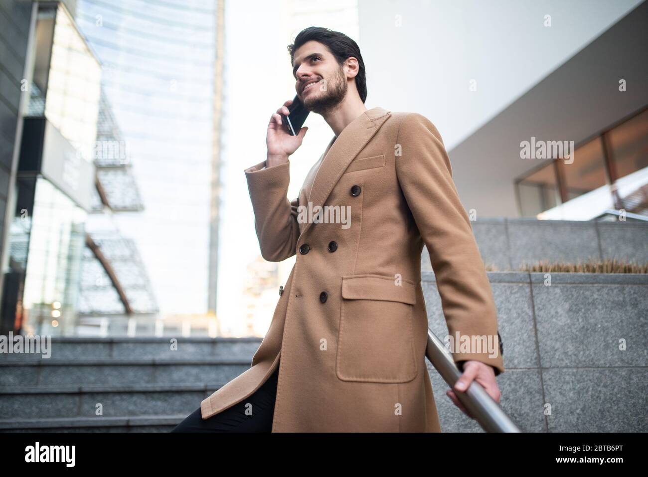 Smiling man talking on the phone while walking down a stair Stock Photo ...