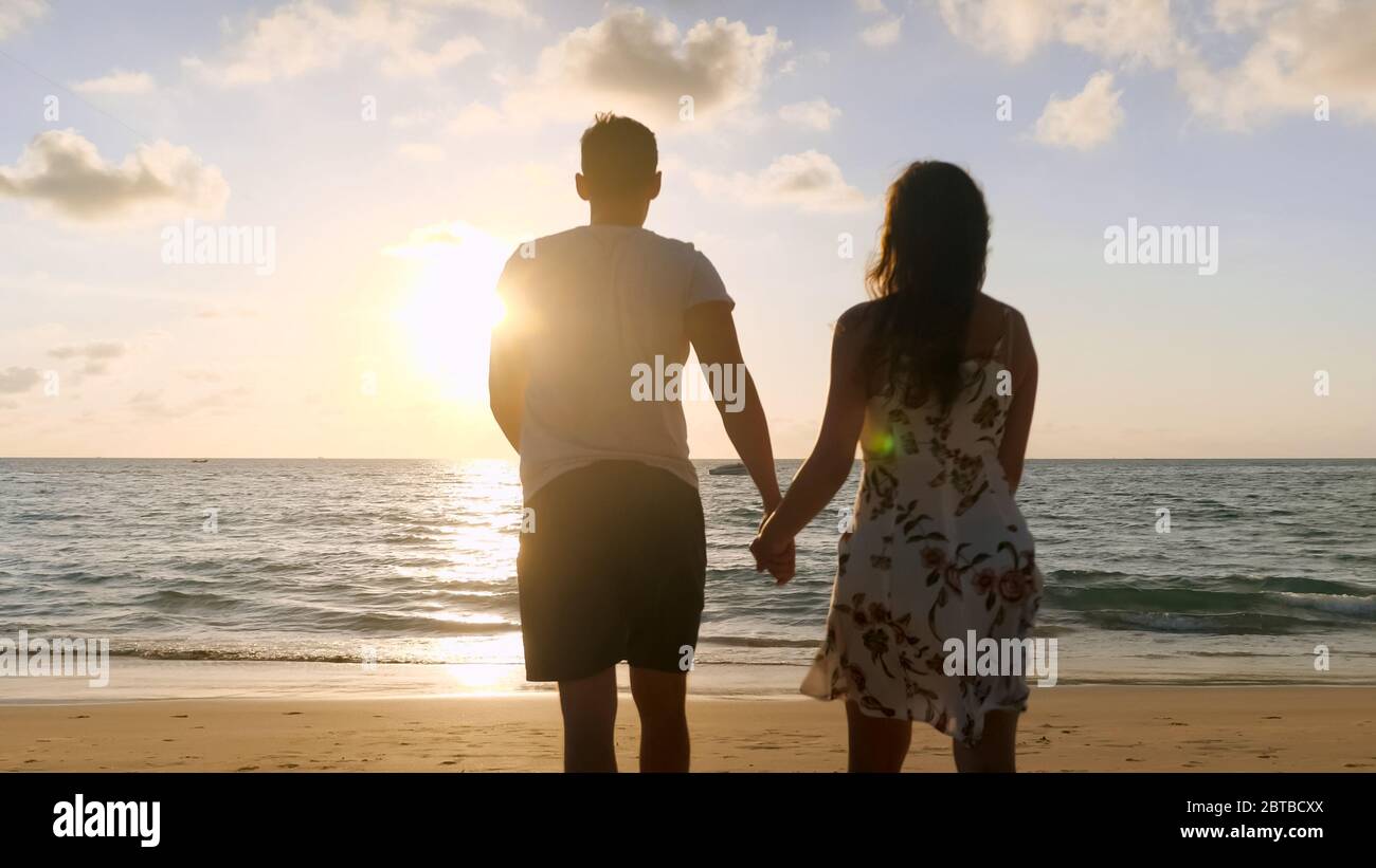 silhouette of happy couple walking joining hands along beach to ocean ...