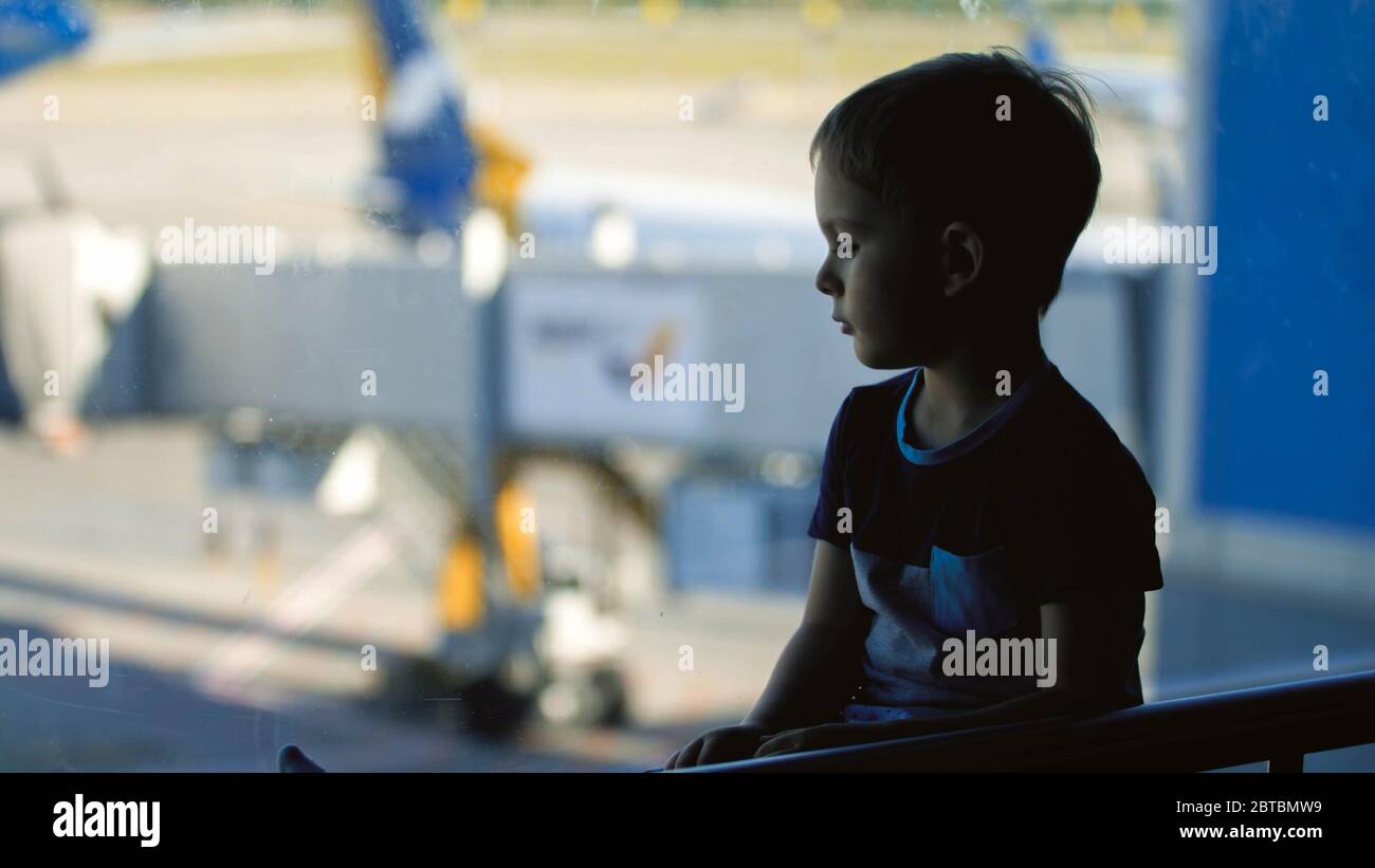 Portrait of sad little boy sitting at big window in airport terminal ...