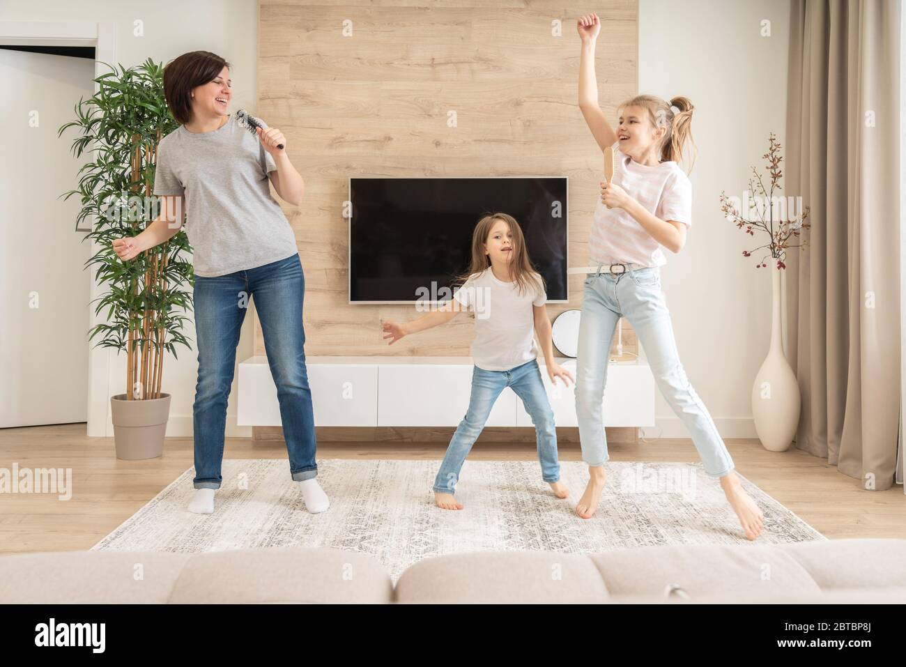Happy mother and two daughters having fun singing karaoke song in hairbrushes. mother laughing ...