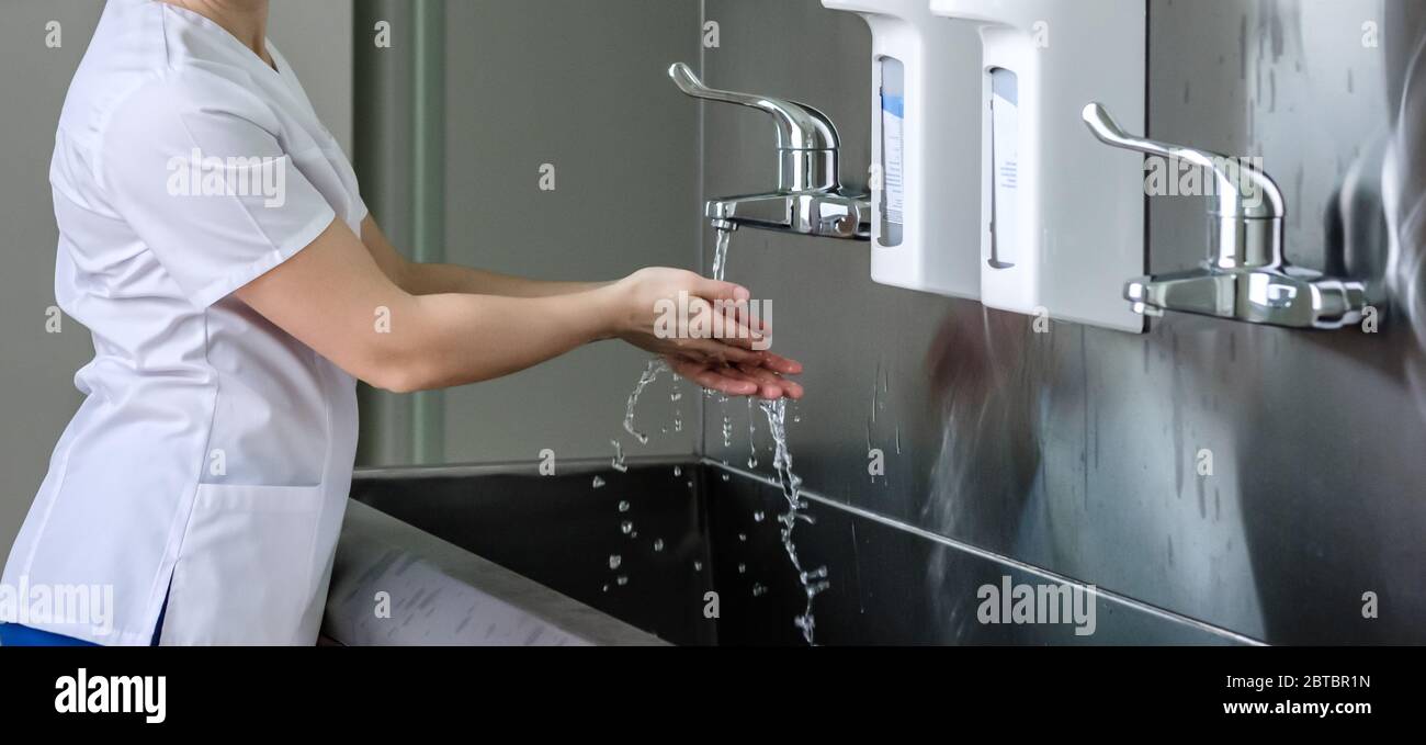 The doctor washes his hands under the tap in a stainless steel sink ...