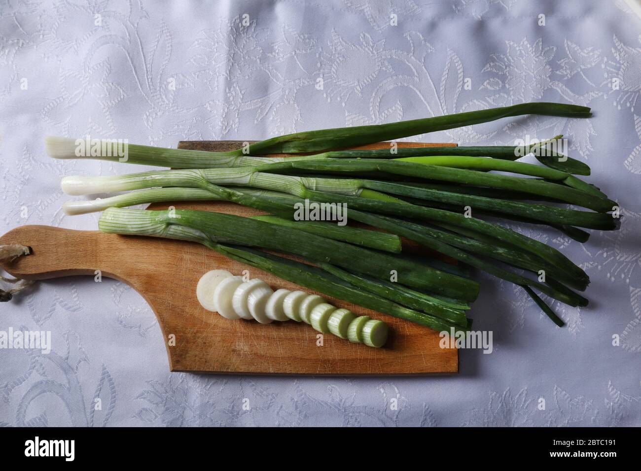 Young onion stalks and pieces of chopped onion on a wooden kitchen ...