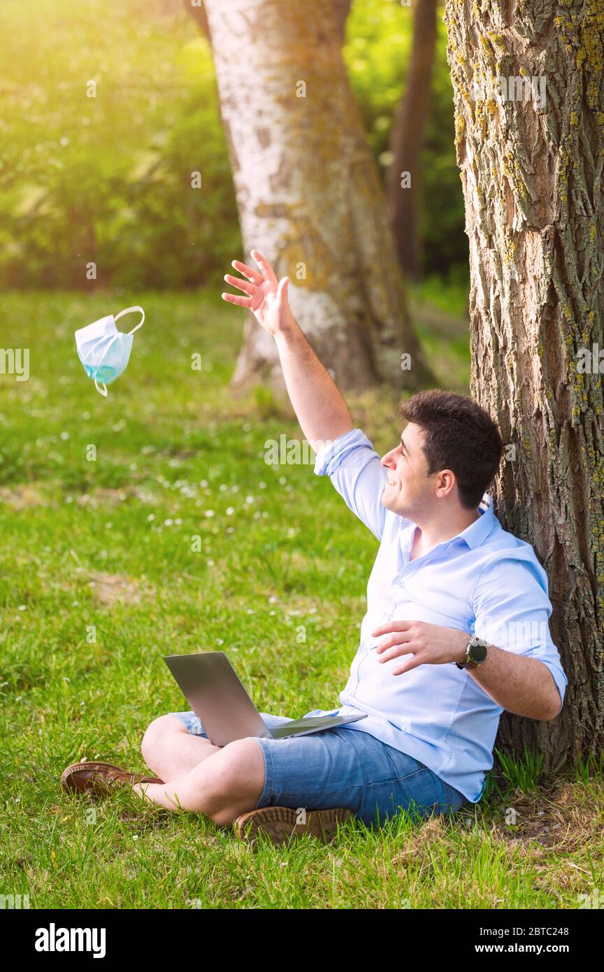 Young man sitting in the park throwing away protective face mask ...