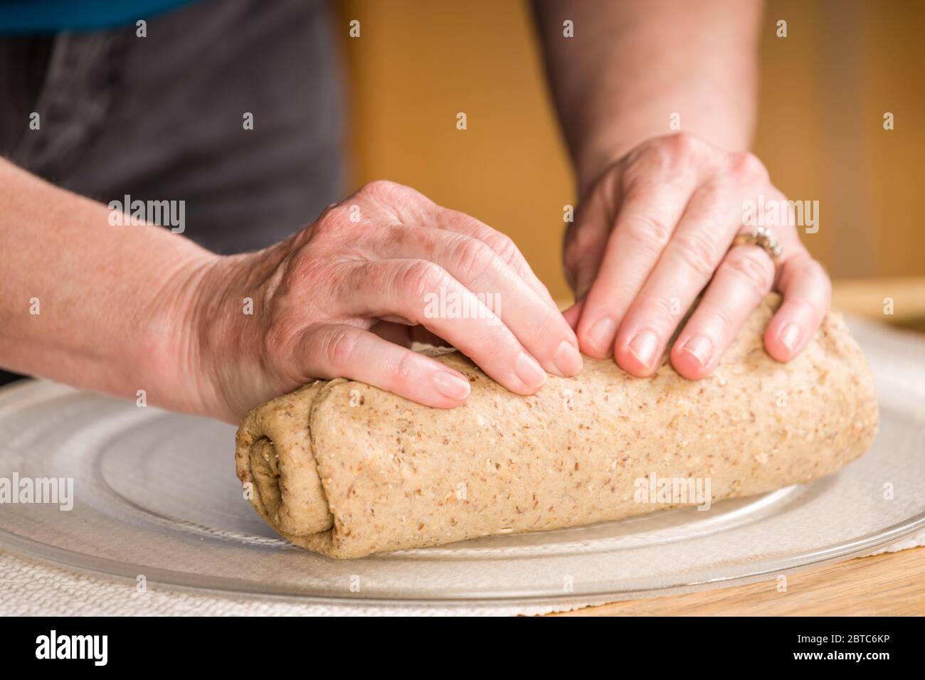 Woman rolling flattened multi-grain bread dough jelly-roll style to ...