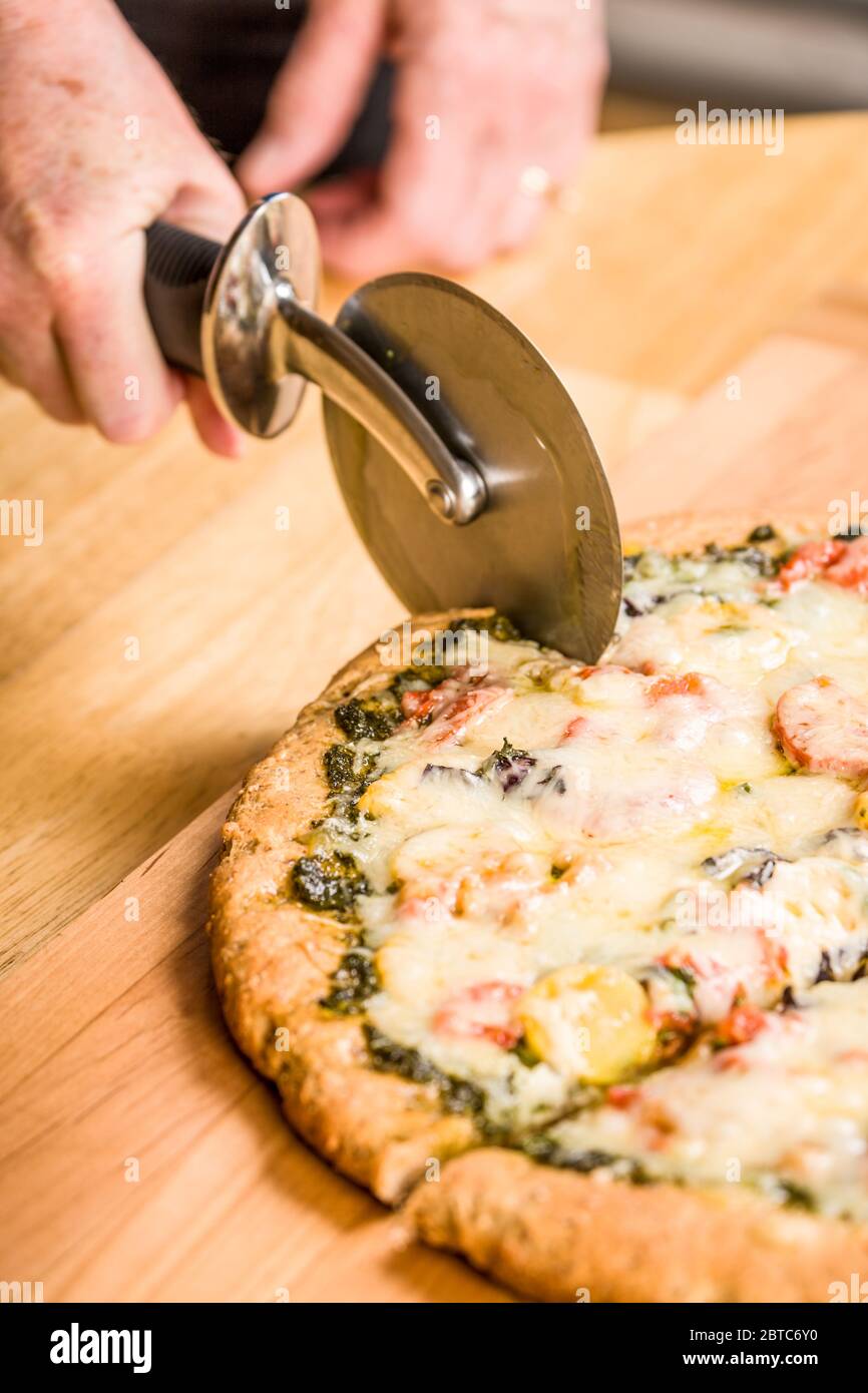 Woman using a pizza cutter to slice a freshly-baked, vegetarian, pesto ...