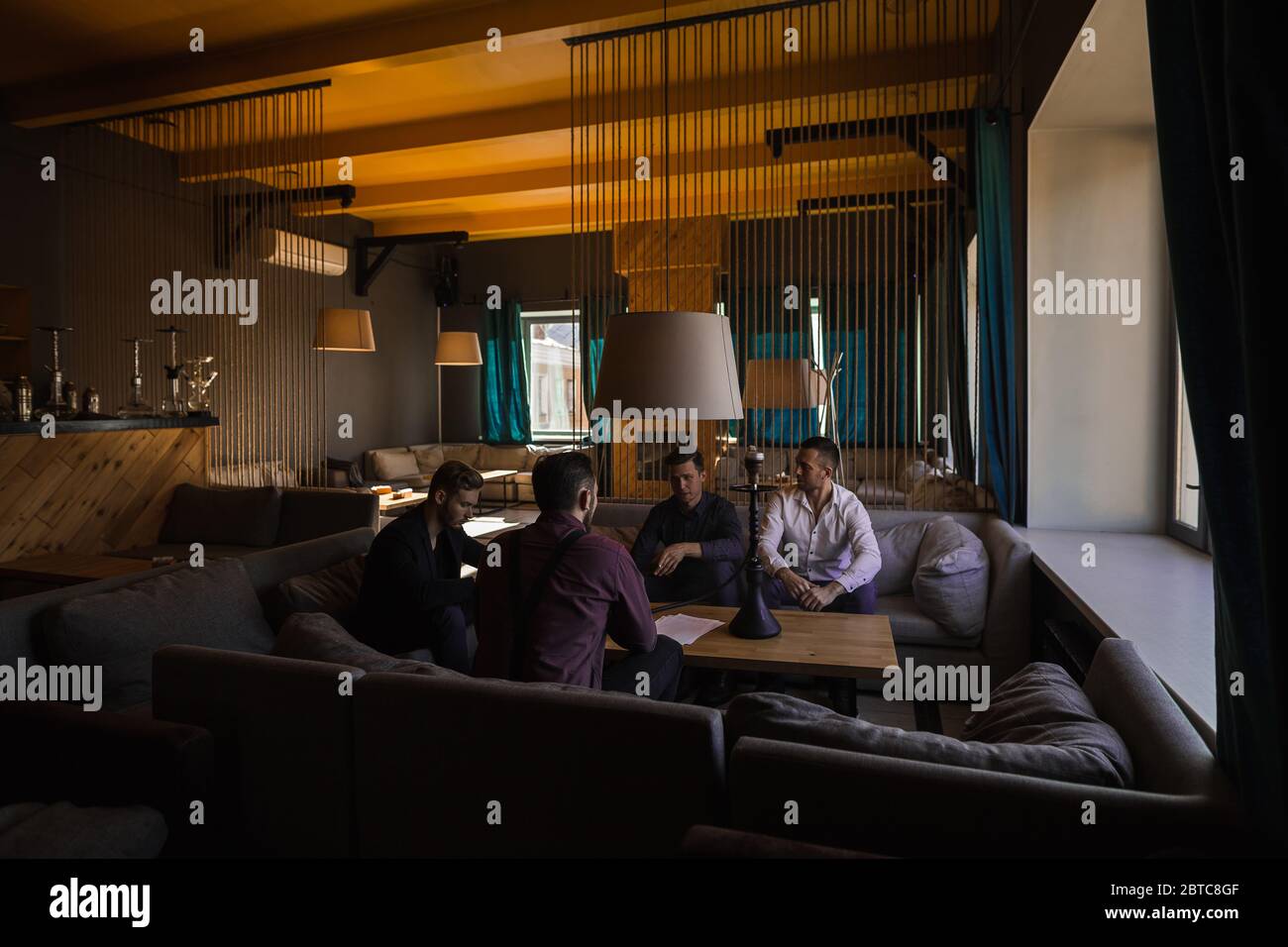 Men relax and smoke hookah in a stylish loft cafe with a modern design ...