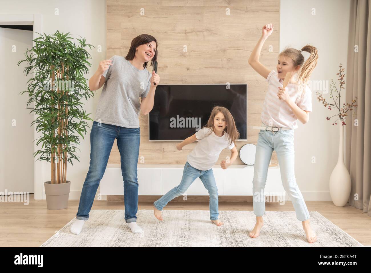 Happy mother and two daughters having fun singing karaoke song in hairbrushes. mother laughing ...