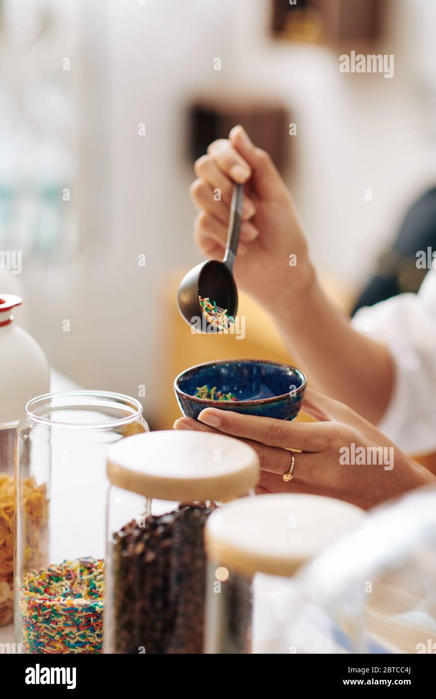 Waiter putting spoon of colorful sprinkles in ceramic bowl with ice ...