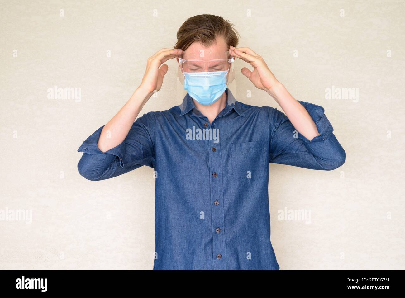 Stressed young man with mask and face shield having headache against ...