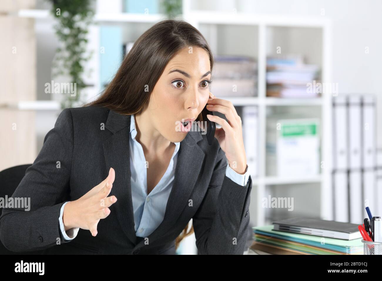 Surprised executive woman calling on smart phone sitting on a desk at ...