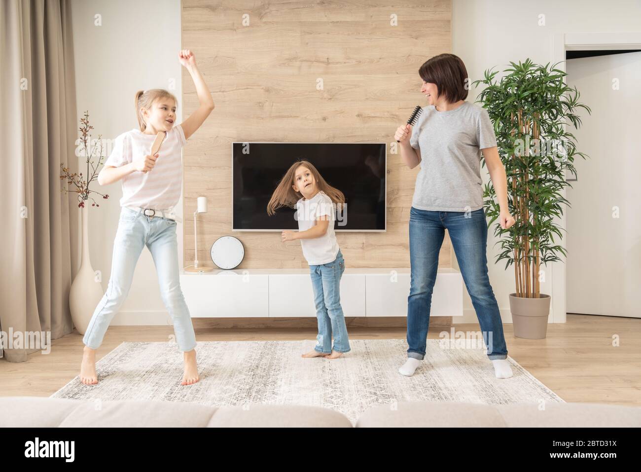 Happy mother and two daughters having fun singing karaoke song in hairbrushes. mother laughing ...