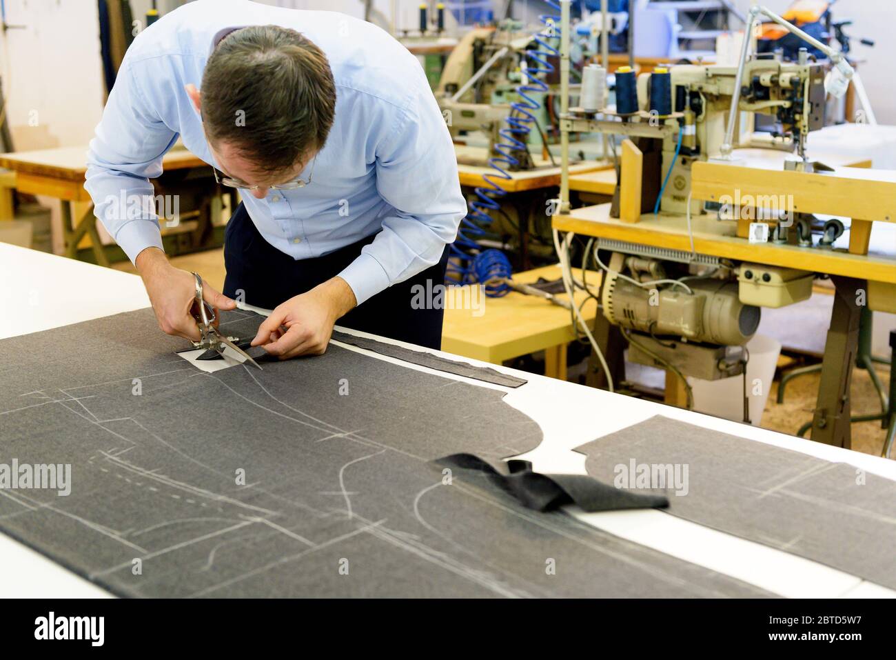 Tailor bending over a workbench cutting fabric on which a pattern has ...