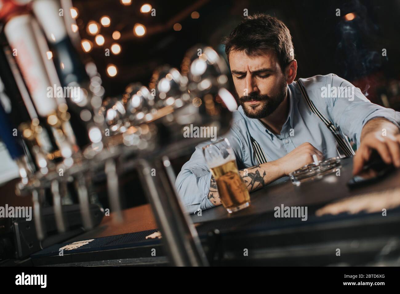 Young man drinking beer and smoking cigarette at pub in the night club ...
