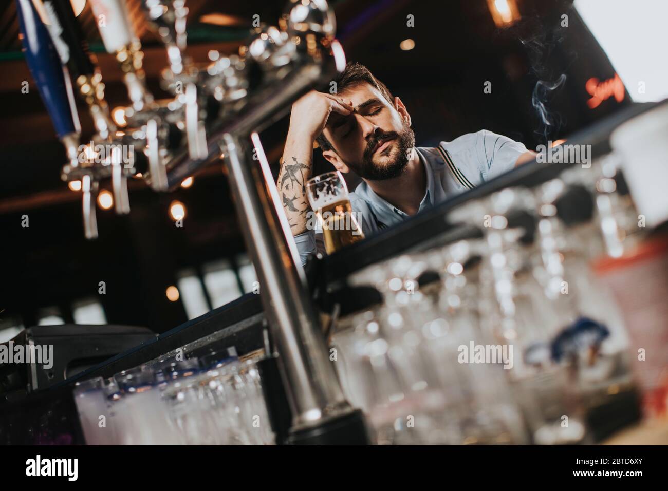 Young man drinking beer and smoking cigarette at pub in the night club ...