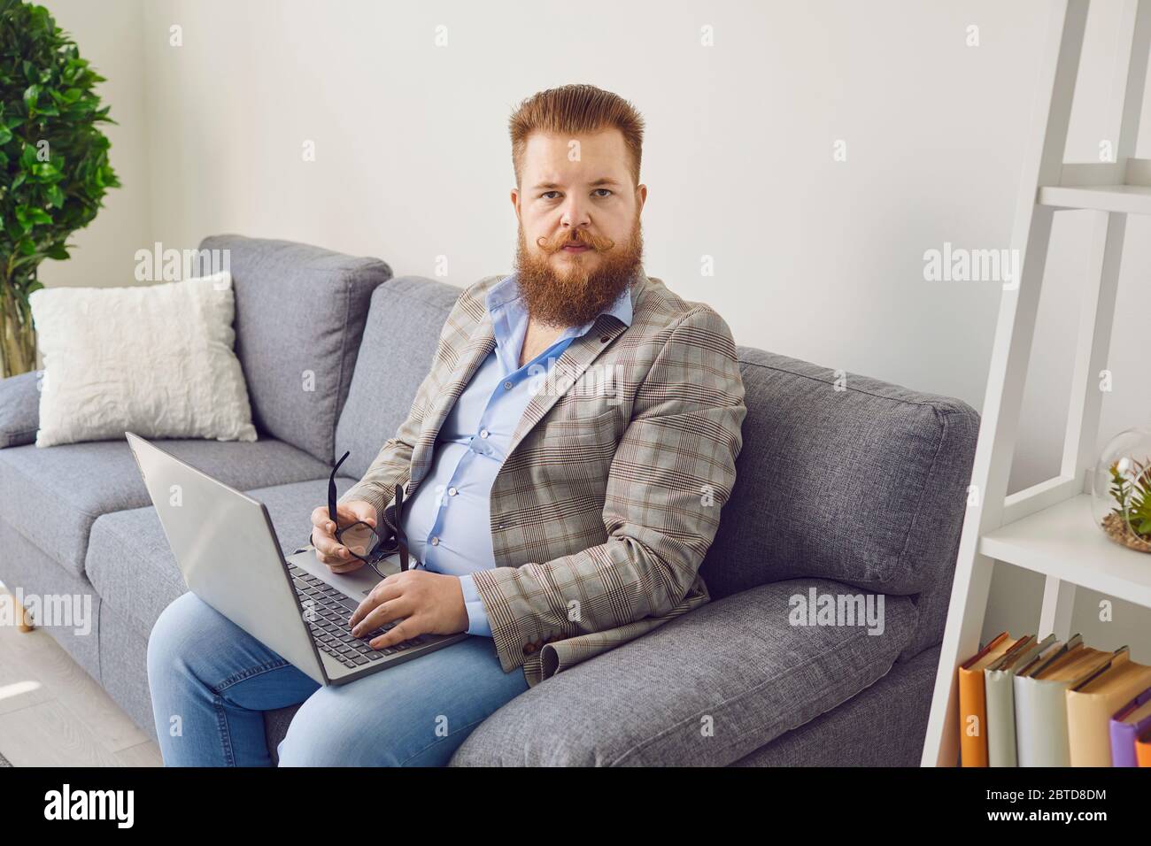 Work online at home office. Funny fat man works using a laptop in the ...