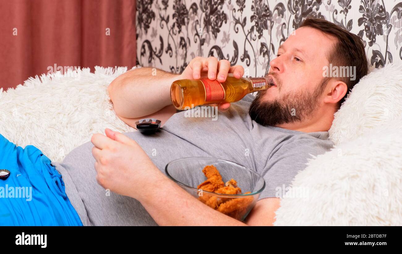 fat man drinks beer and eats unhealthy food chicken wings, bored in ...