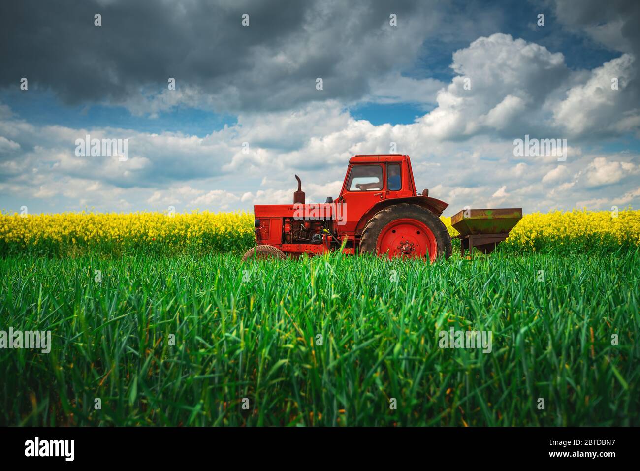 Red tractor in a field and dramatic clouds Stock Photo - Alamy