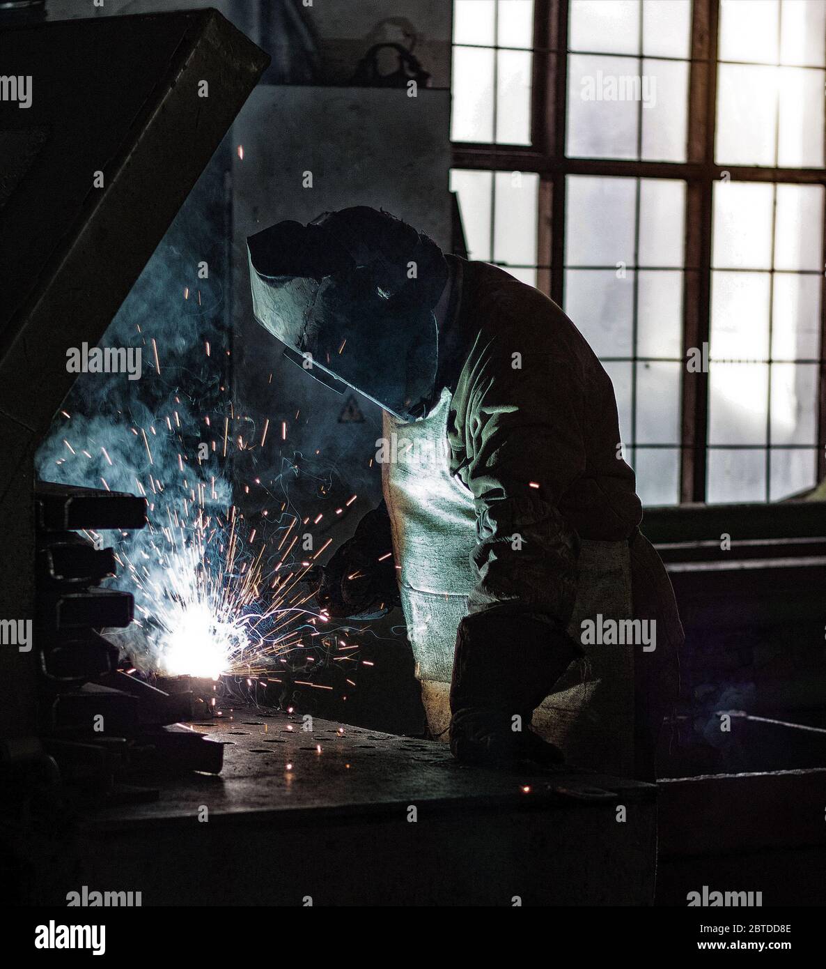 Welder at the factory welds metal parts, welding and sparks, dirty ...
